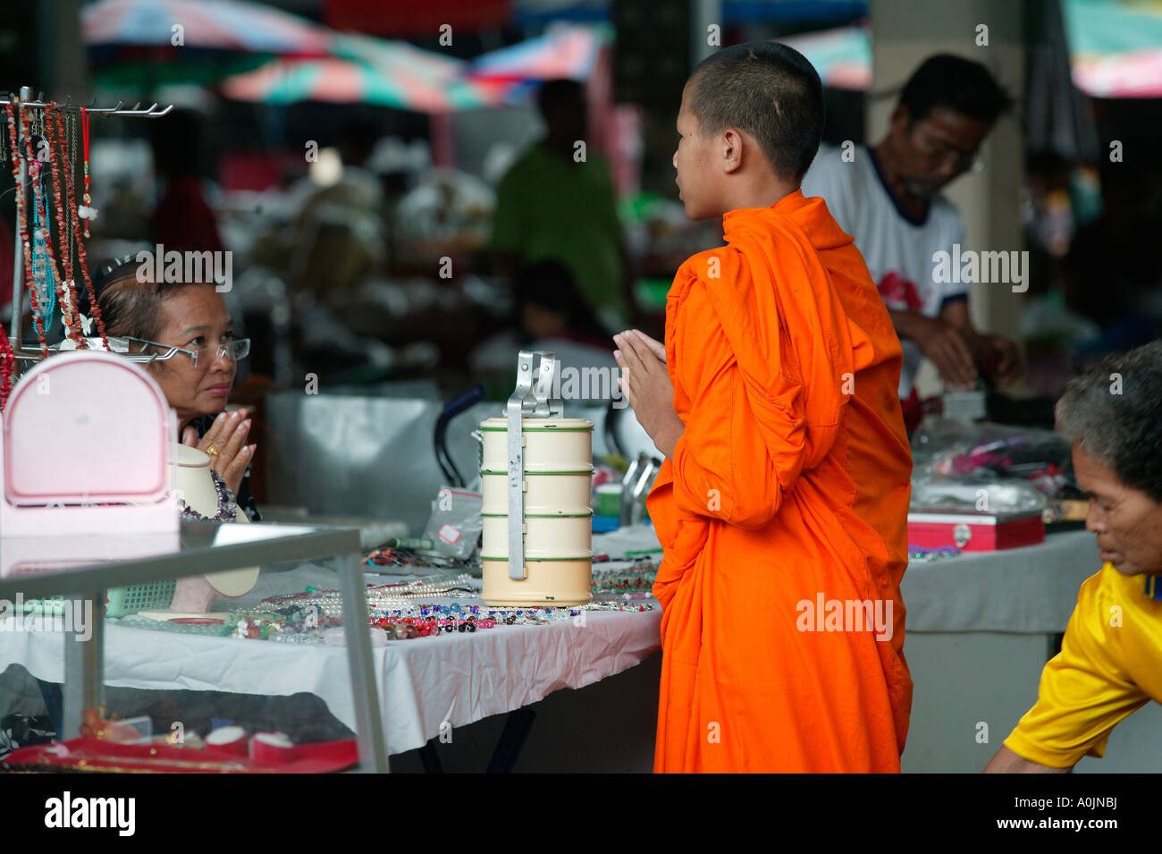 A young Buddhist monk and a lady stall holder in a market in Khon Kaen ...