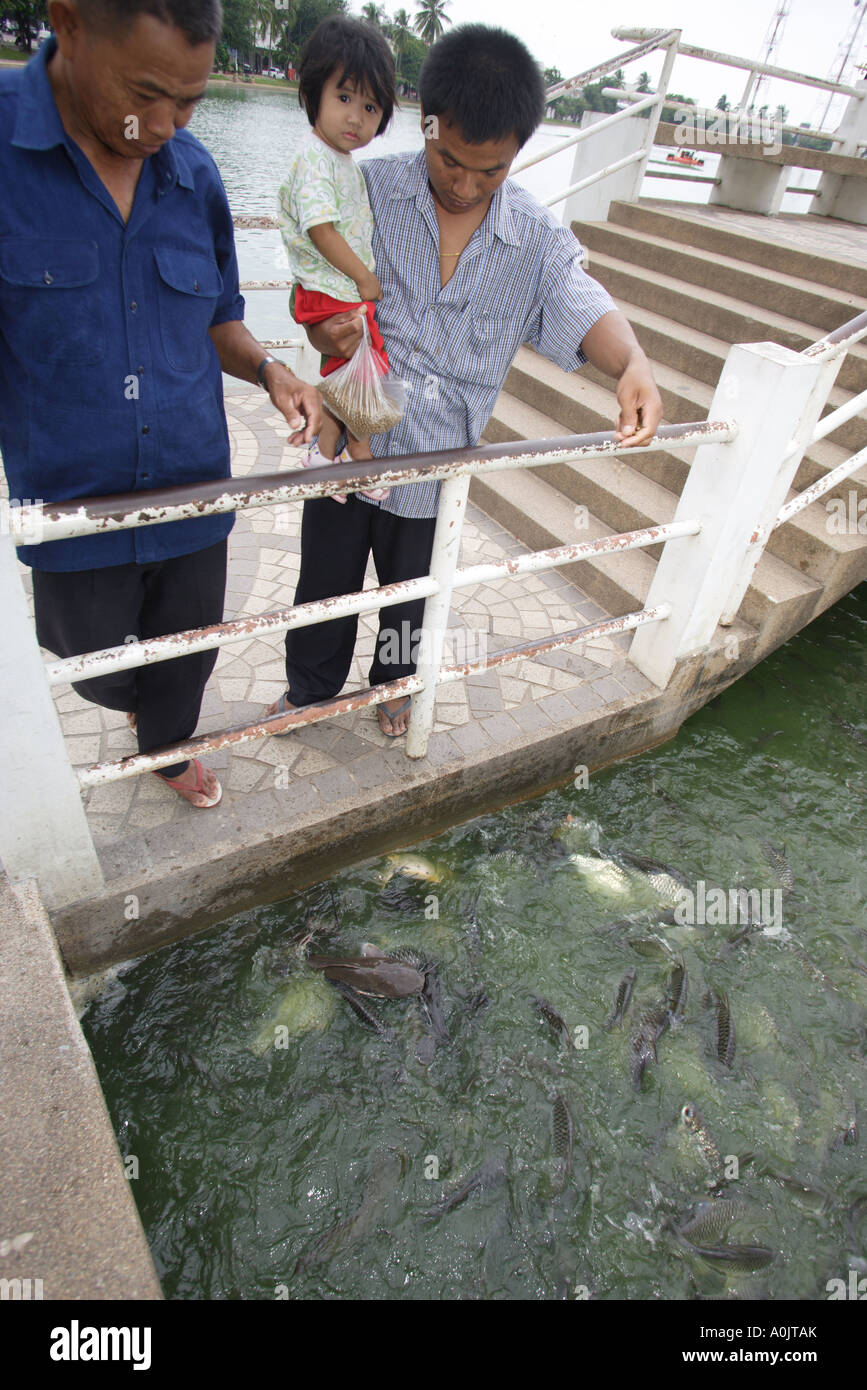 A man and his young daughter feeding fish in Beaung Plan Chai lake in ...