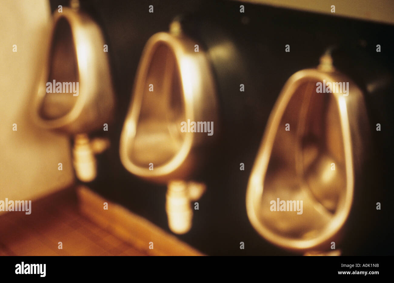 Impressionistic detail of three mens urinals either in a warm copper ...