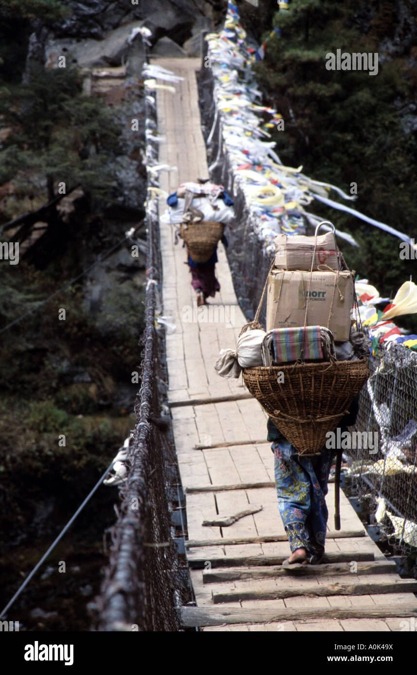 Porters carrying heavy loads over a rope bridge into the high Himalayas ...