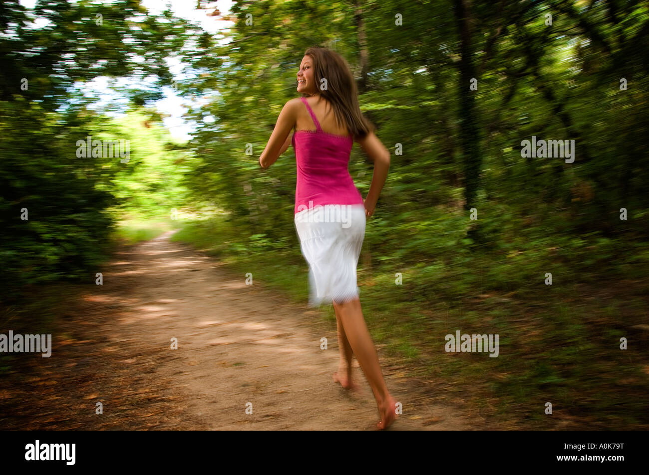 Teen girl 15 yrs old happy running away and looking back on a path ...