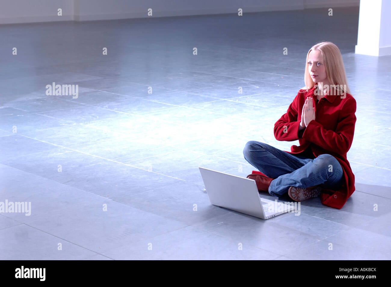 young woman sitting on floor with computer making prayer gesture Stock ...