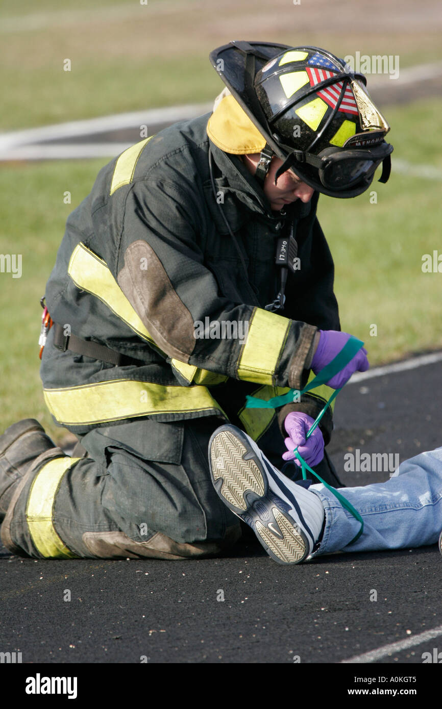 An EMT is wrapping a green colored ribbon to the leg of a victim laying ...