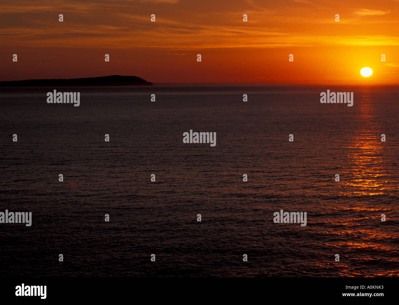 Deep orange sunrise with the sun on the horizon reflecting off the sea ...