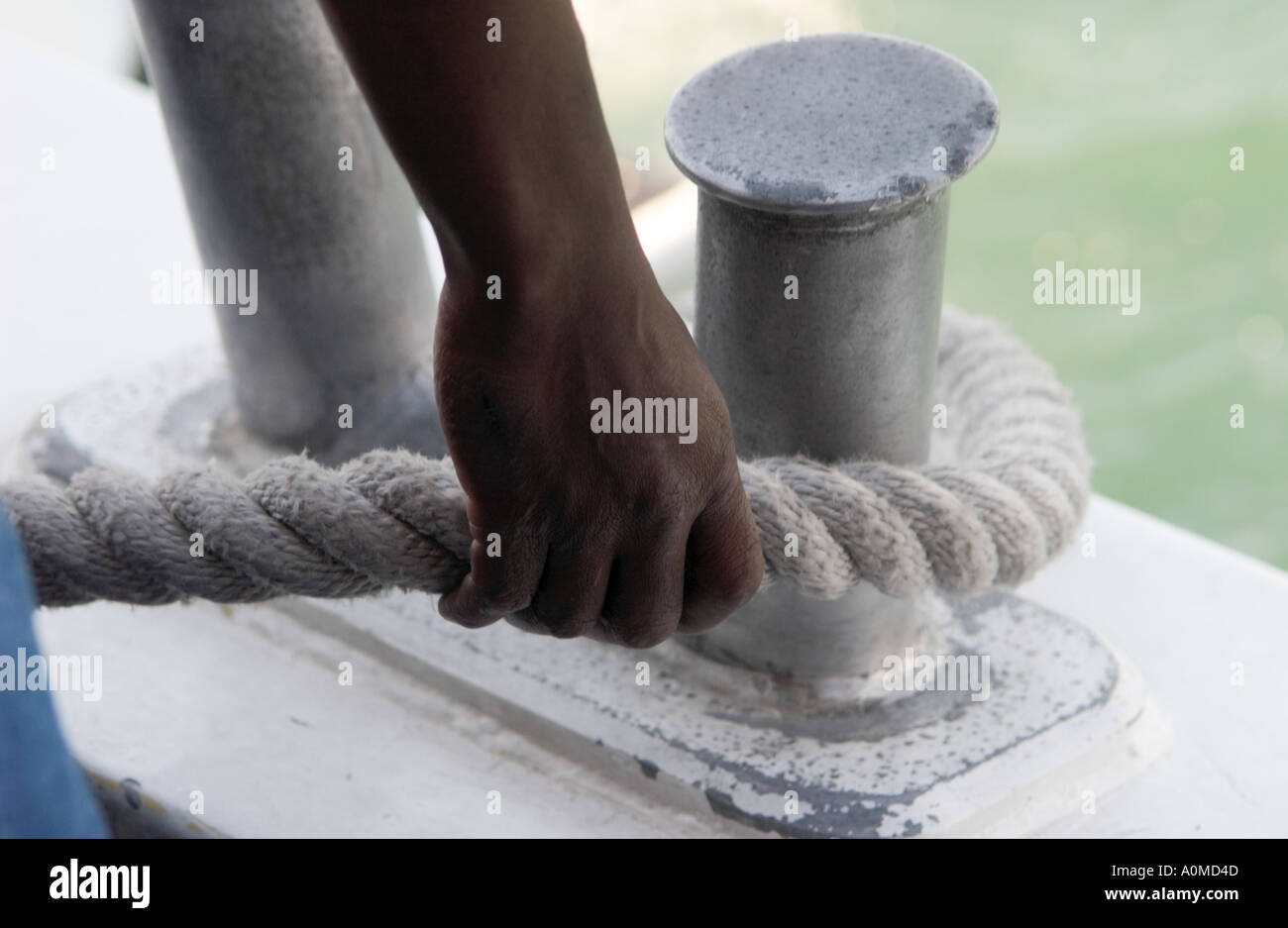 A close up of a young man hand wrapping a thick rope around a mooring ...