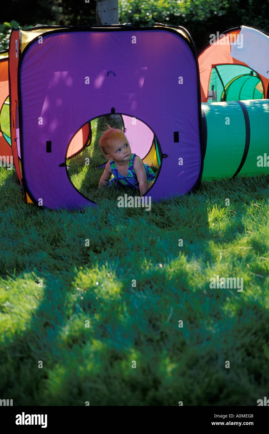 young baby toddler peers from colorful canvas tent tube maze backyard ...
