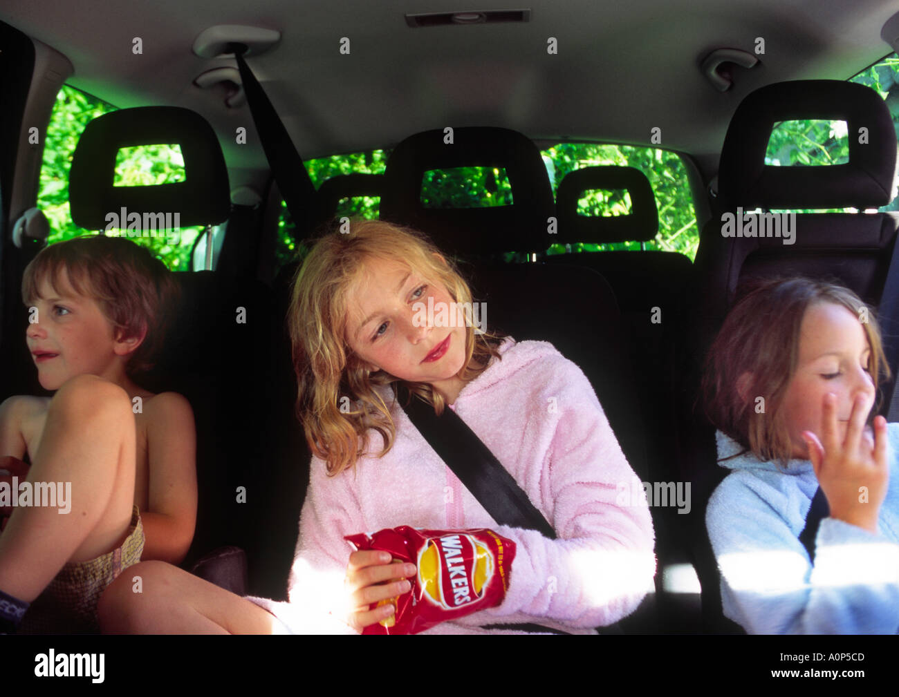 three children in the car with seatbelts on, eating crisps and looking ...