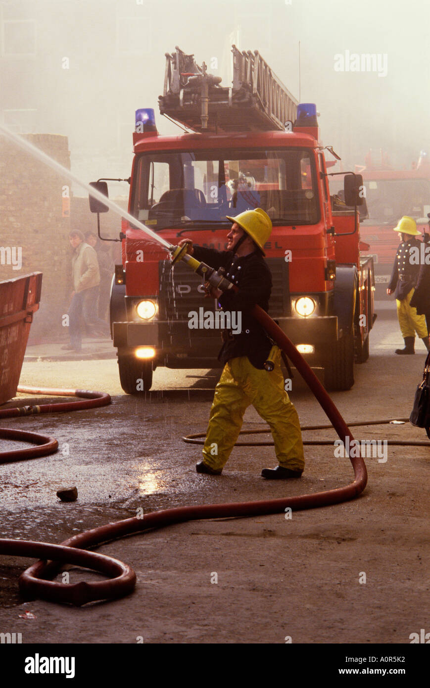 Fireman spraying water from firehose with fire engine in background ...