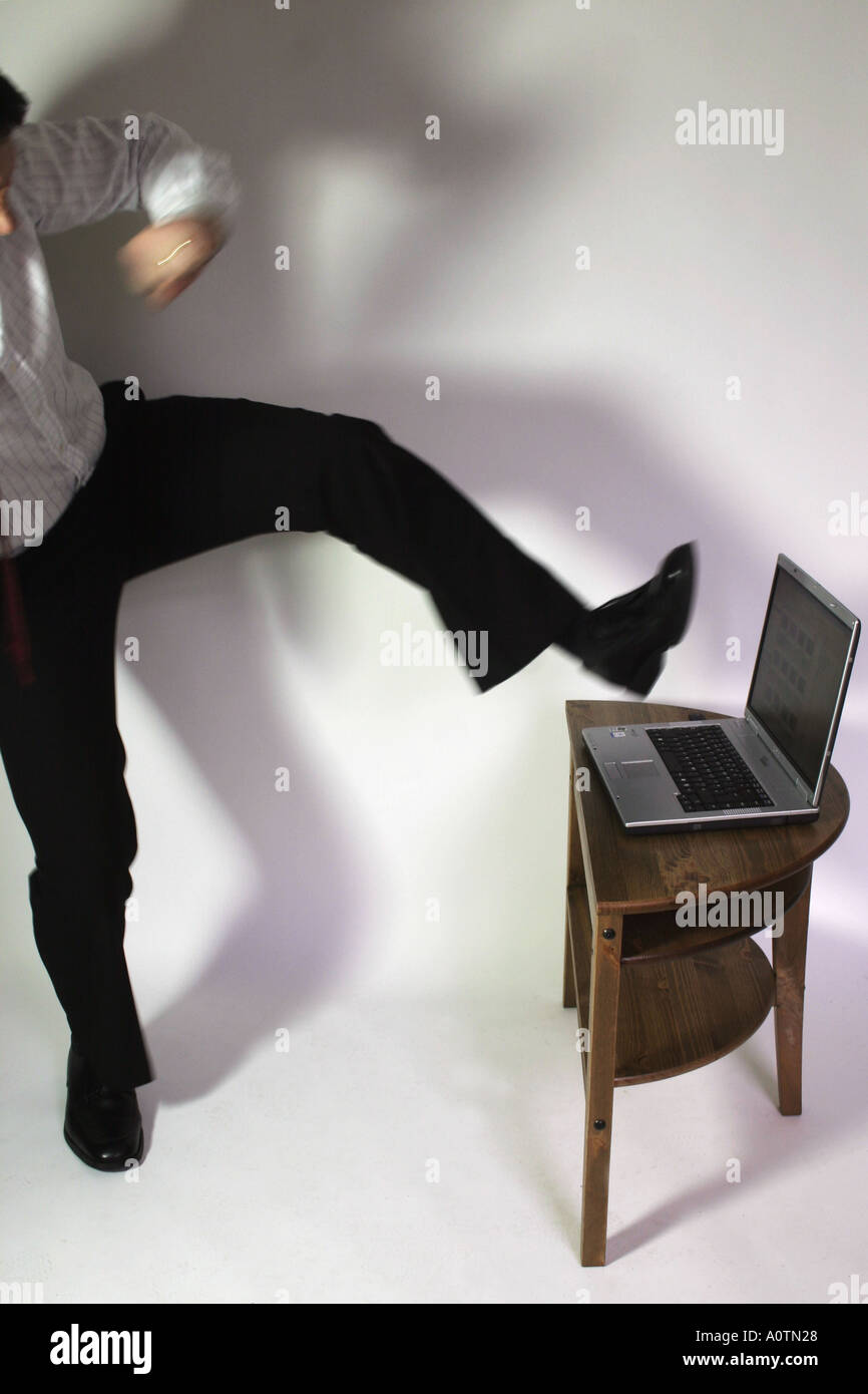 Conceptual image showing business man kicking out at a lap top computer ...