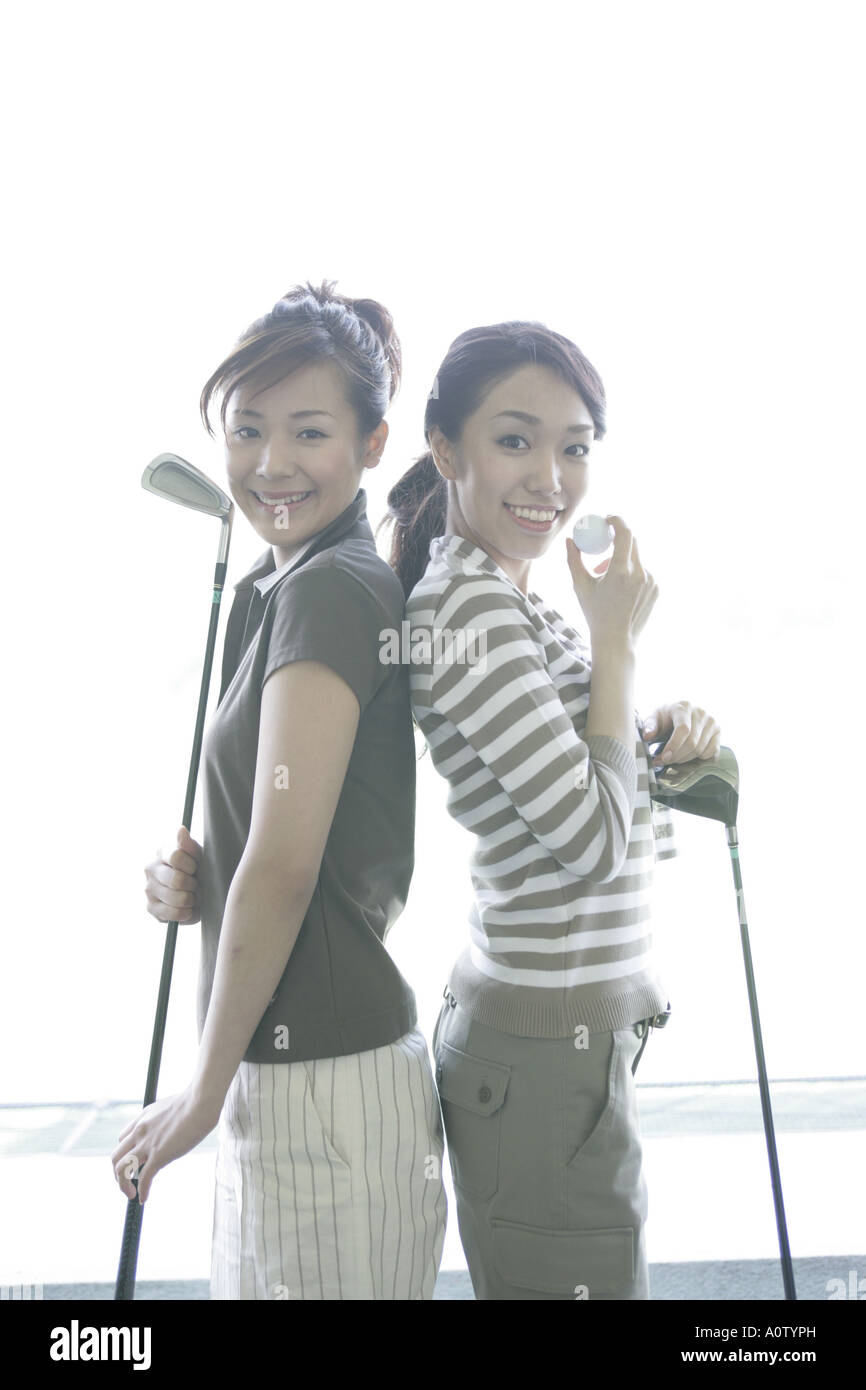 Portrait of two young women standing back to back and holding golf ...