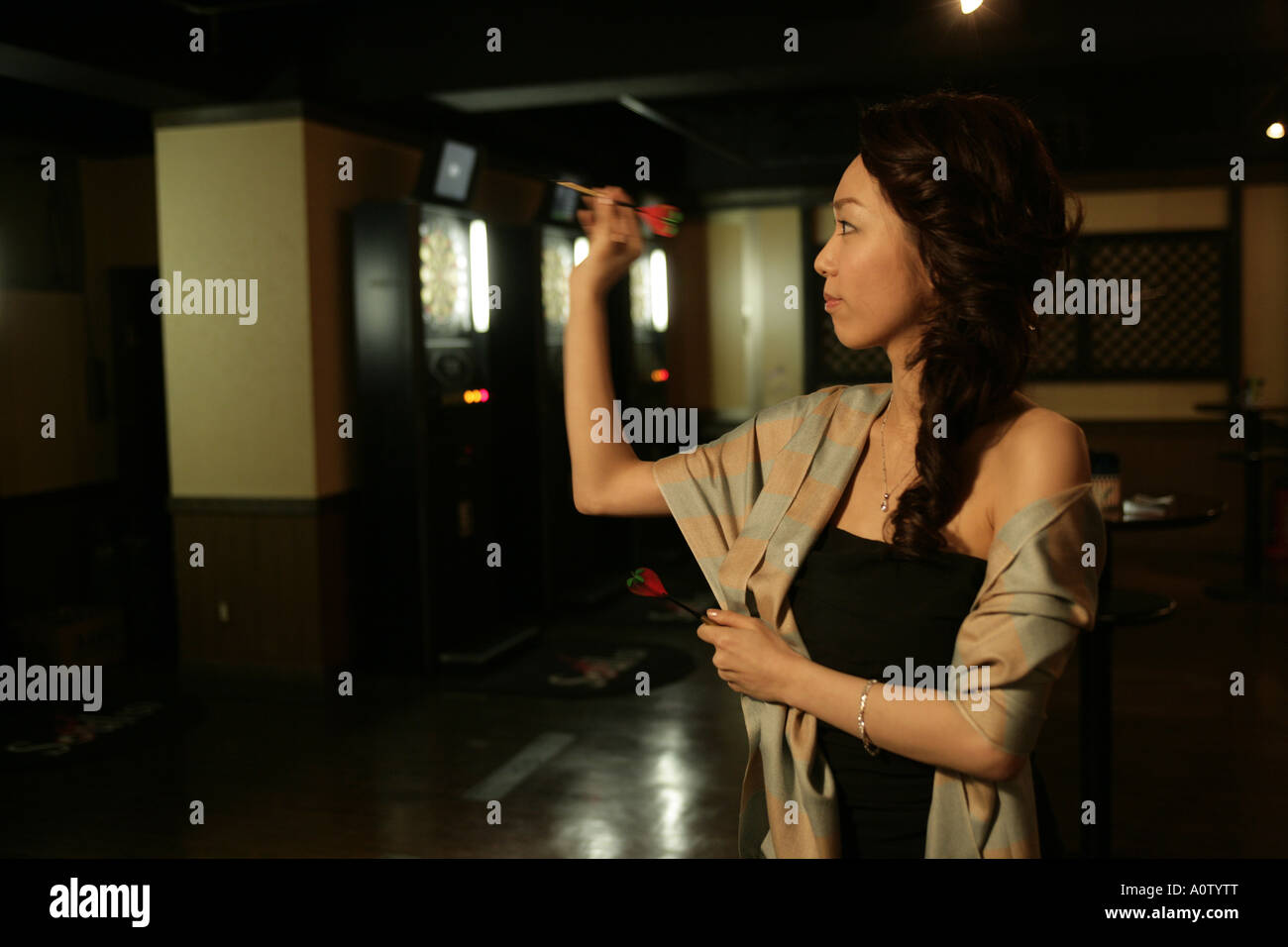 Young woman holding a dart and aiming at a dart board in a nightclub ... Young woman holding a dart and aiming at a dart board in a nightclub ...