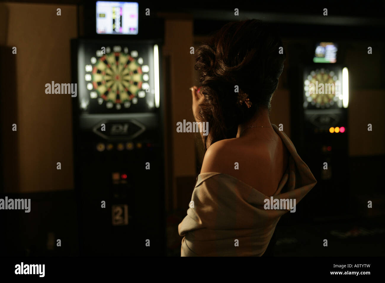 Rear view of a young woman holding a dart and aiming at a dart board ...