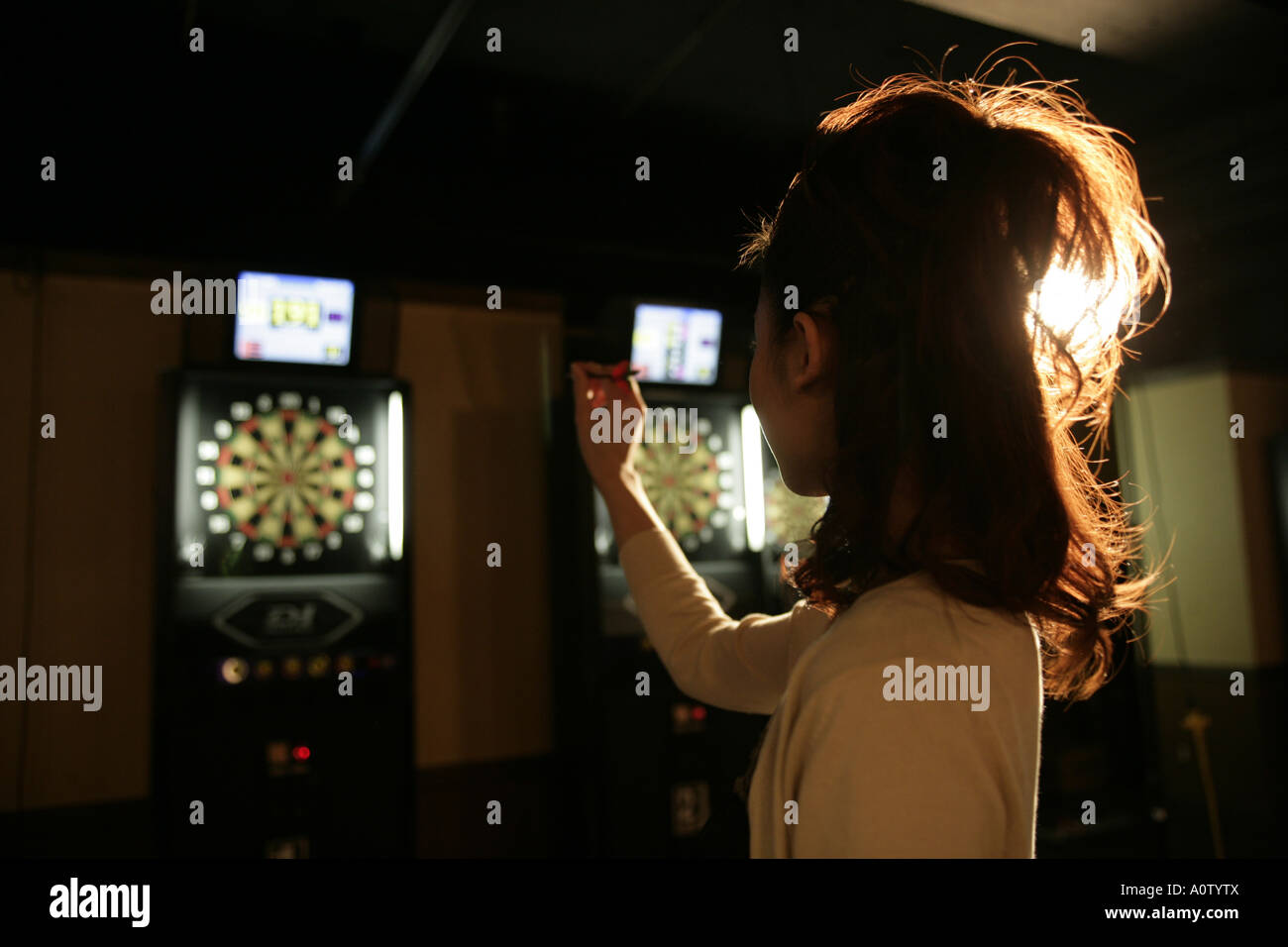 Side profile of a young woman holding a dart and aiming at a dart board ...