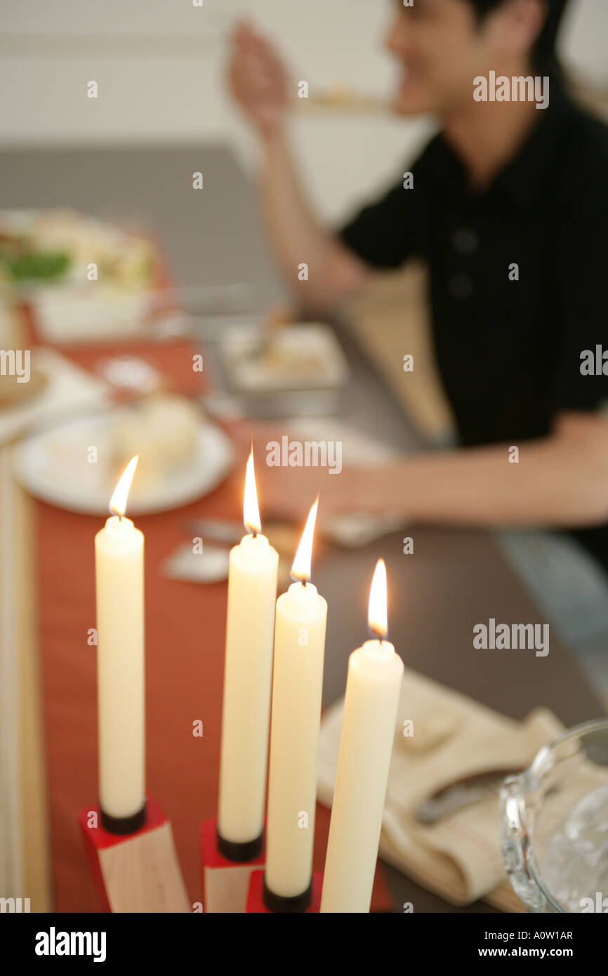 Close up of four lit candles on a dining table with a man eating in the ...
