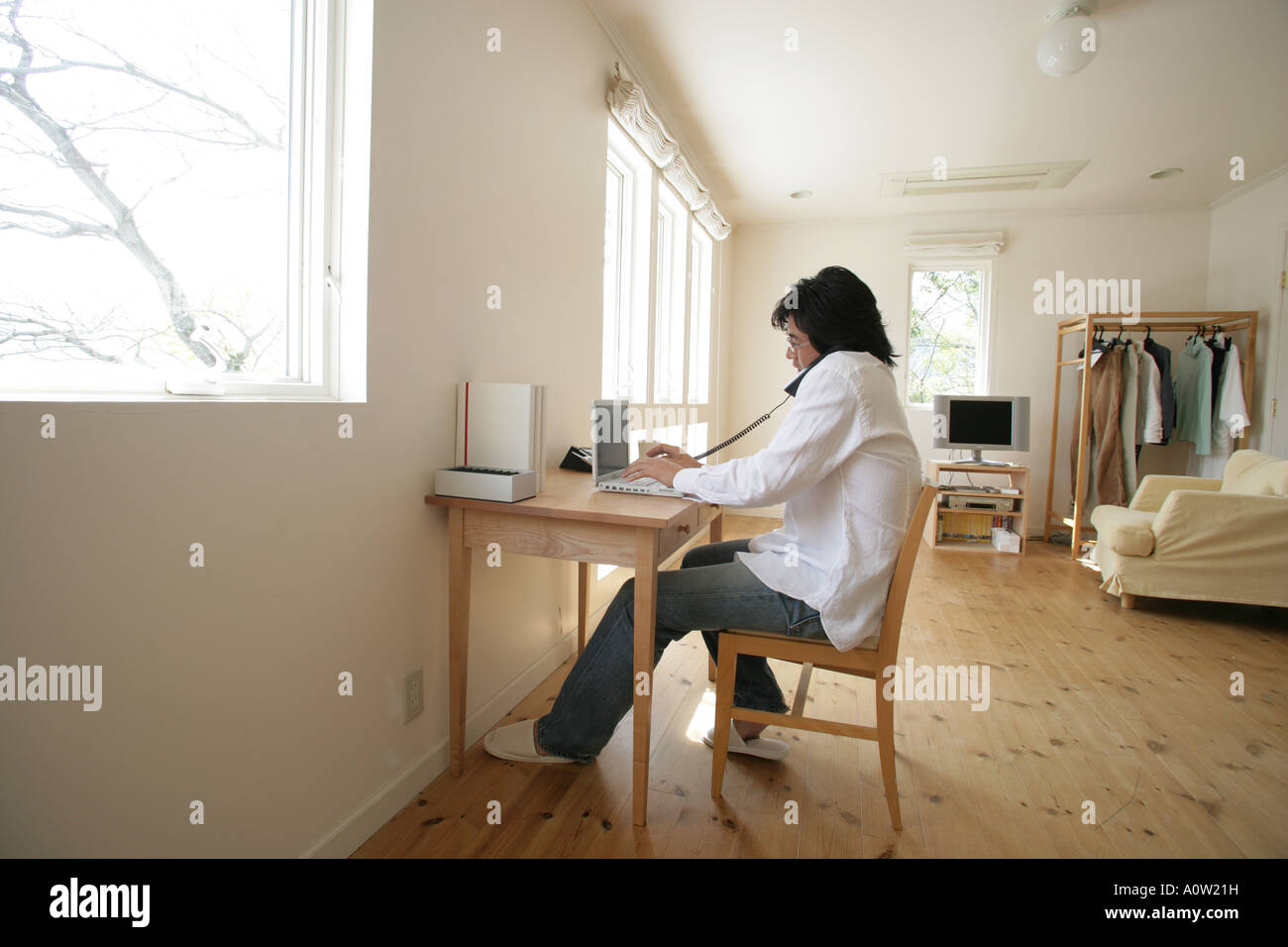 Side profile of a young man using a laptop and talking on the telephone ...