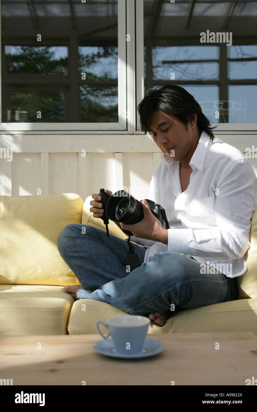 Young man sitting on a couch and holding a camera Stock Photo - Alamy