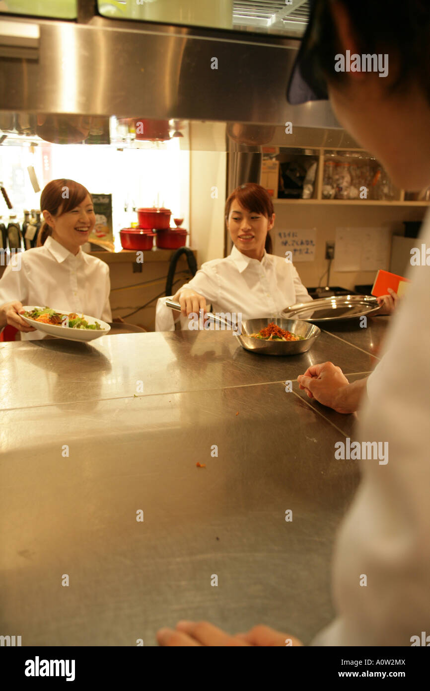 Two waitresses standing at a kitchen counter and serving food Stock ...