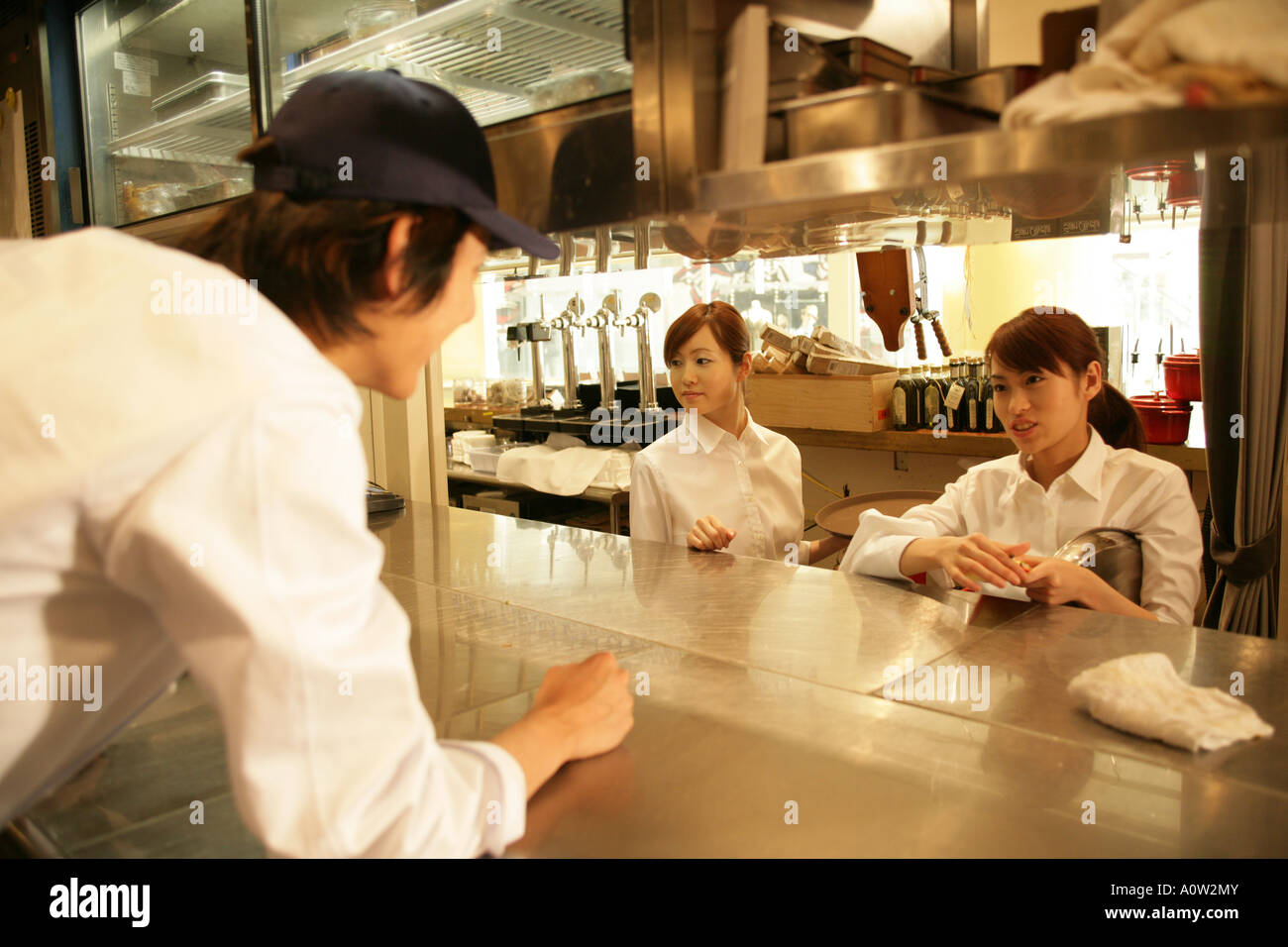 Two waitresses standing at a kitchen counter and talking with a chef ...
