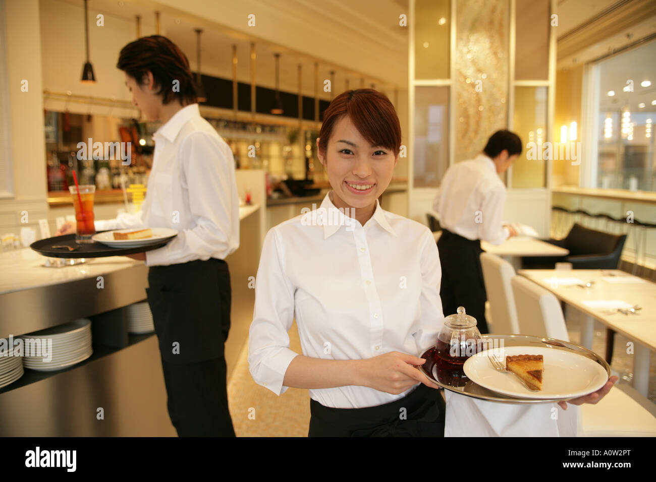 Portrait of a waitress standing in the kitchen with two waiters in the ...
