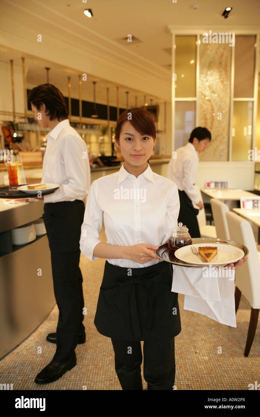 Portrait of a waitress standing in the kitchen with two waiters in the ...