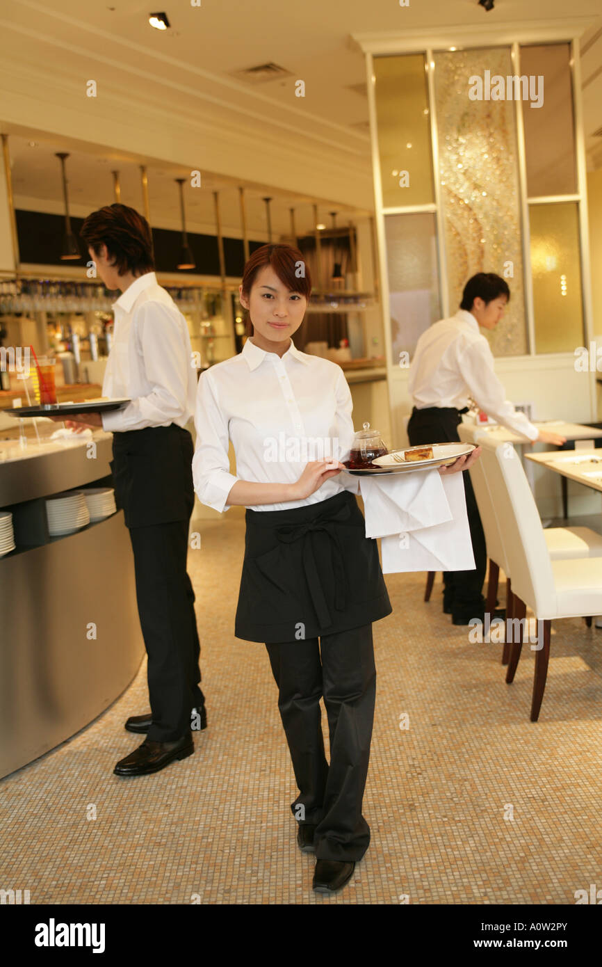 Portrait of a waitress standing in the kitchen with two waiters in the ...