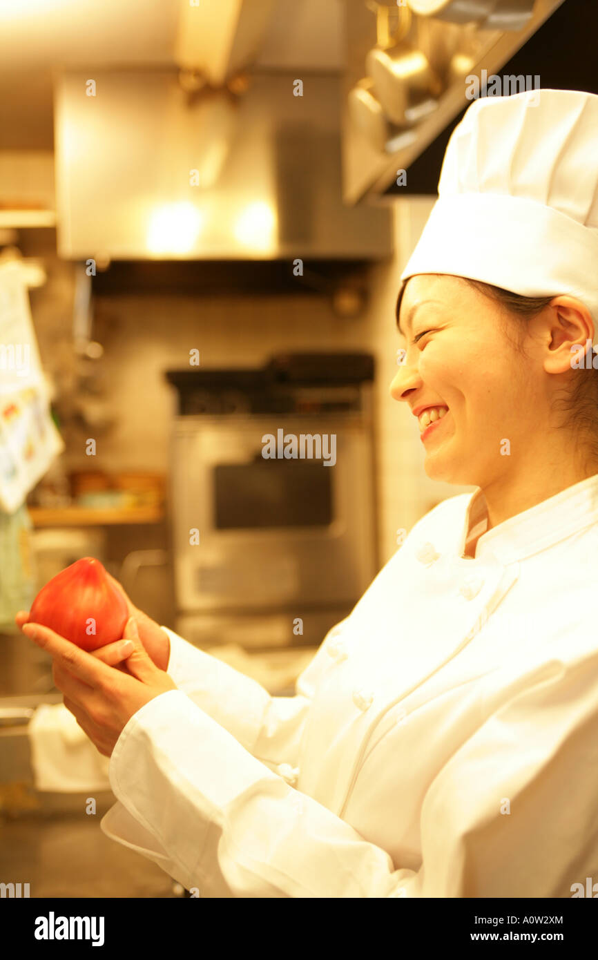 Side profile of a female chef holding a tomato and smiling Stock Photo ...