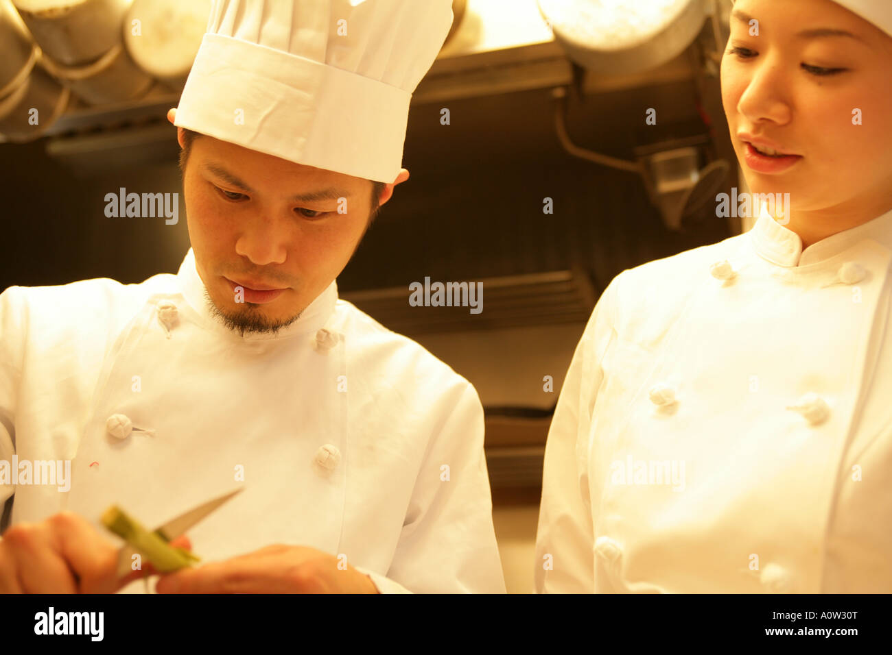 Close up of a male chef cutting vegetable with a female chef looking at ...