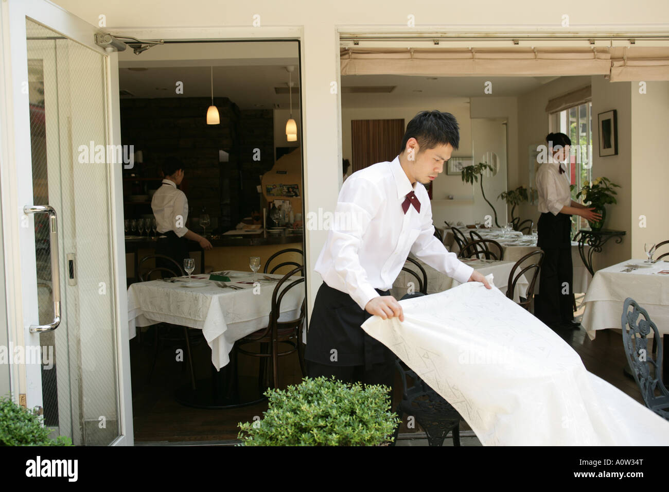 Waiter adjusting a tablecloth in a restaurant with two waitresses in ...