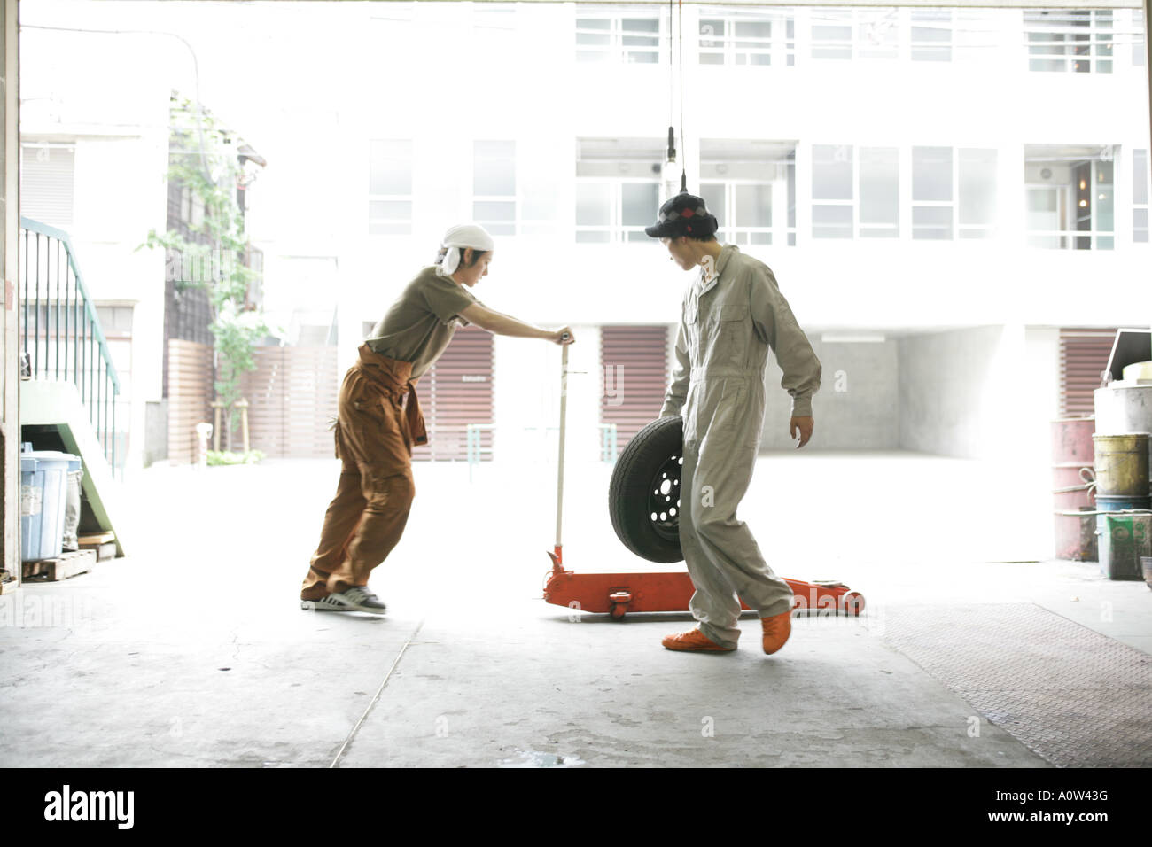 Side profile of an auto mechanic holding a tire with a mechanic pushing ...