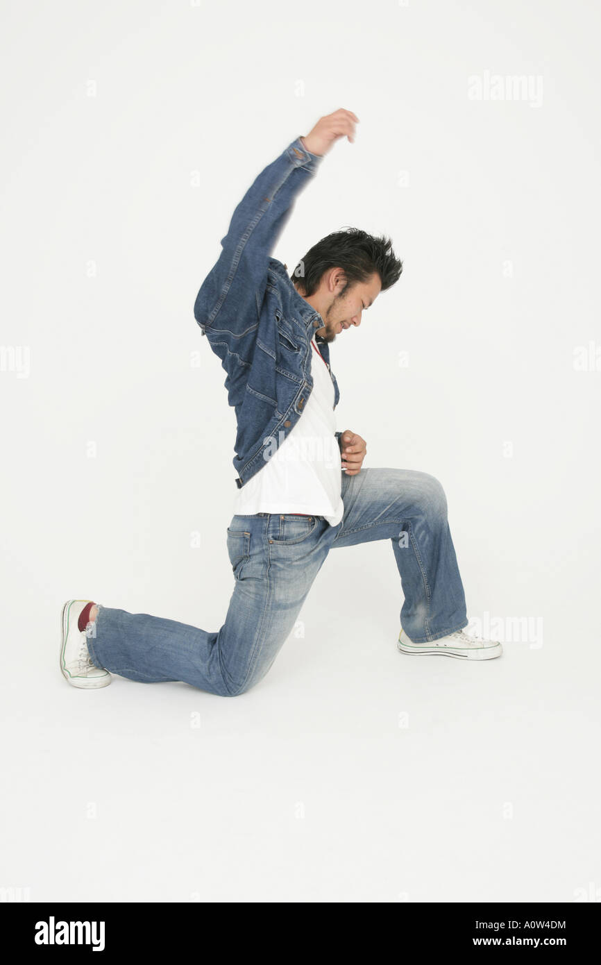 Side profile of a young man kneeling on the floor with one hand raised ...