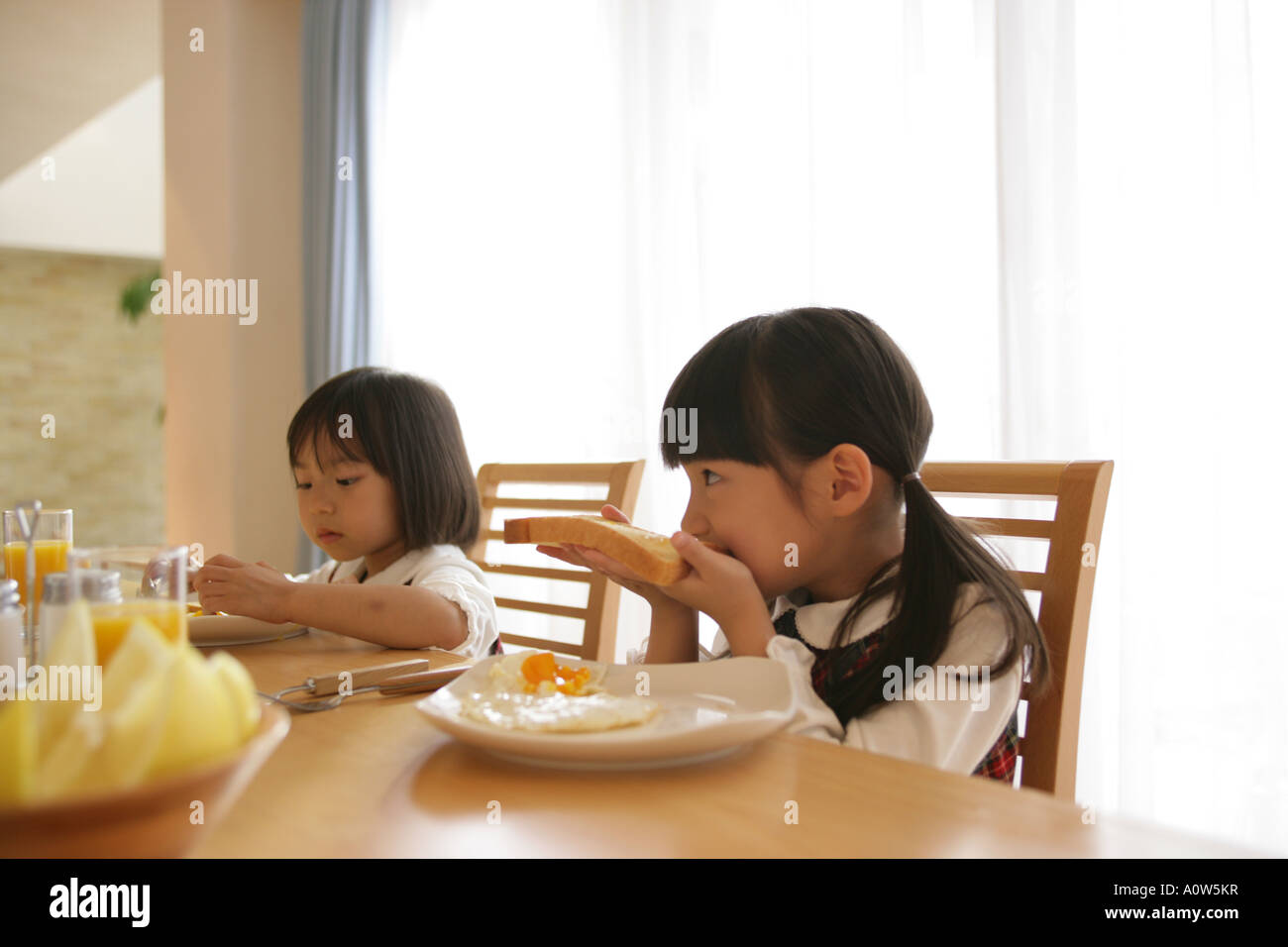 Two girls having breakfast at the dining table Stock Photo - Alamy