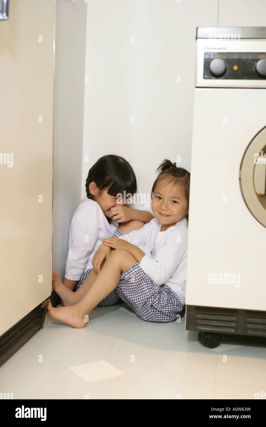 Two girls sitting in a corner near a washing machine Stock Photo - Alamy