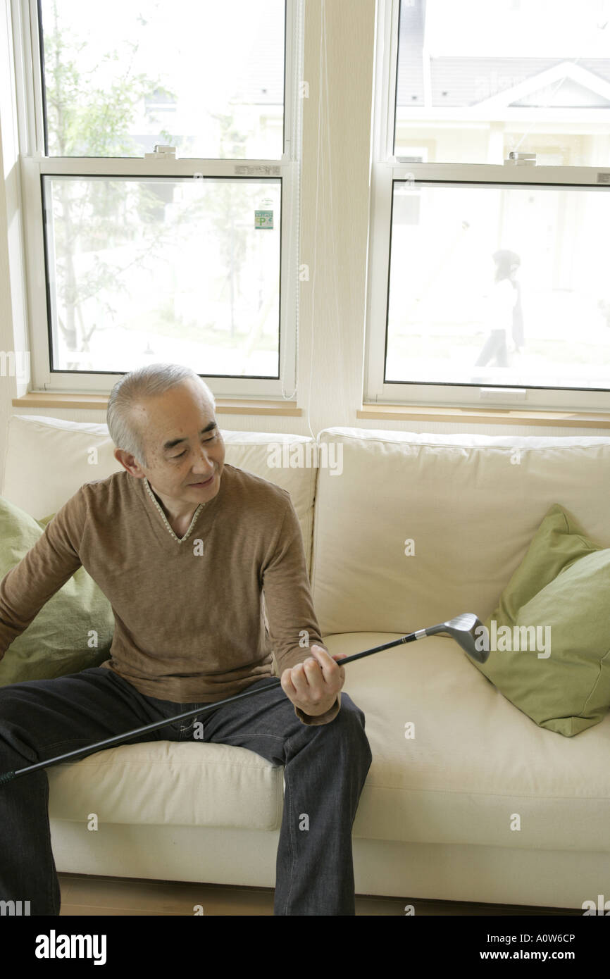 Senior man sitting on a couch and holding a golf club Stock Photo - Alamy
