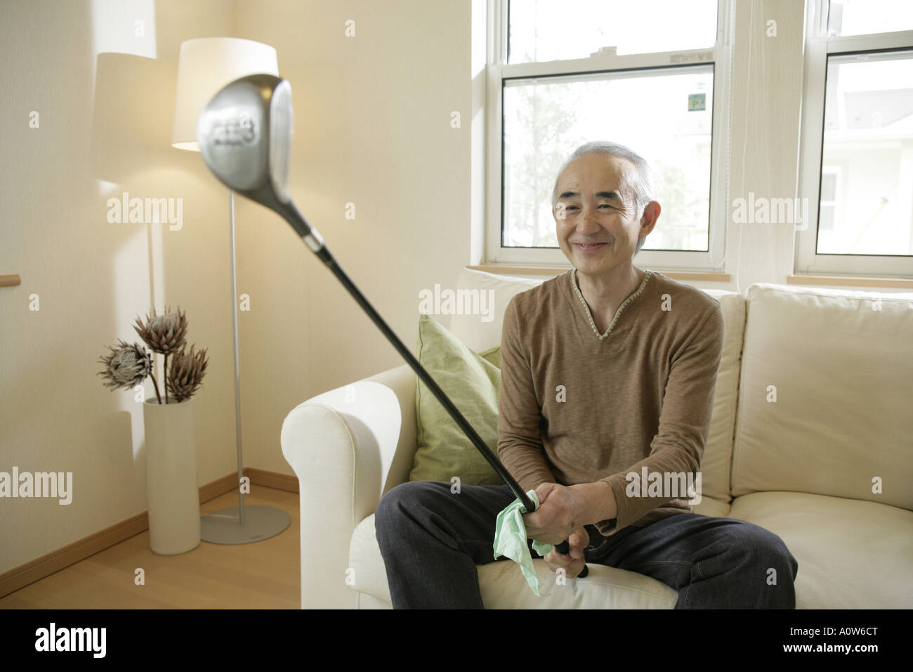 Senior man sitting on a couch and holding a golf club Stock Photo - Alamy