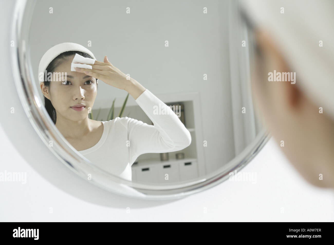 Reflection of a young woman wiping her forehead with a tissue paper in ...
