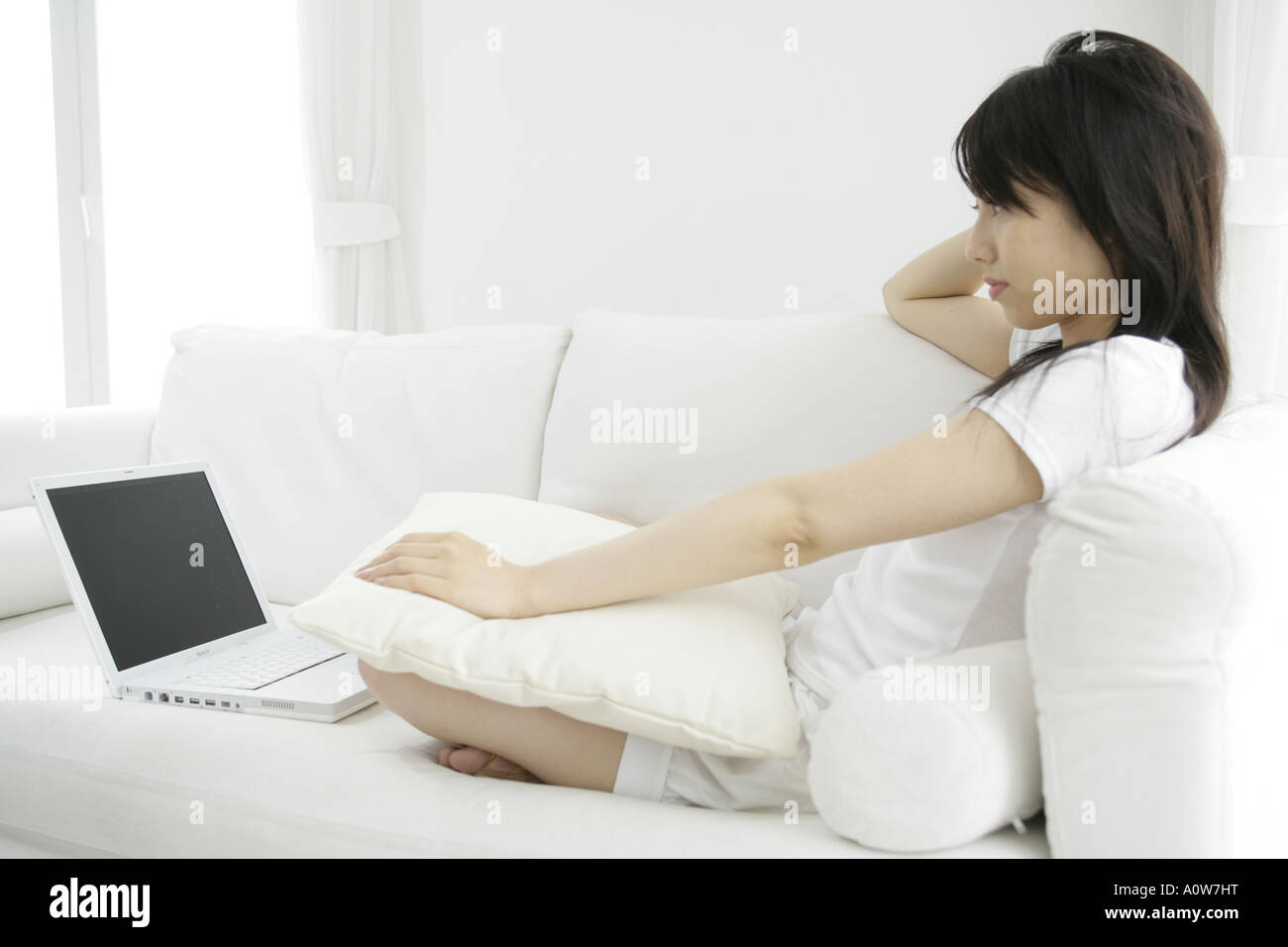 Side profile of a young woman sitting on a couch and using a laptop ...