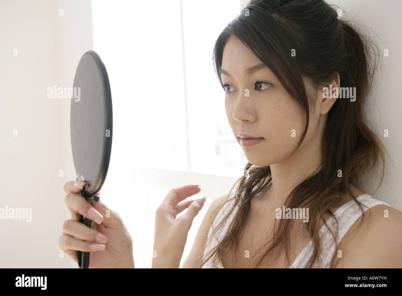 Close up of a young woman looking in a hand mirror and thinking Stock ...