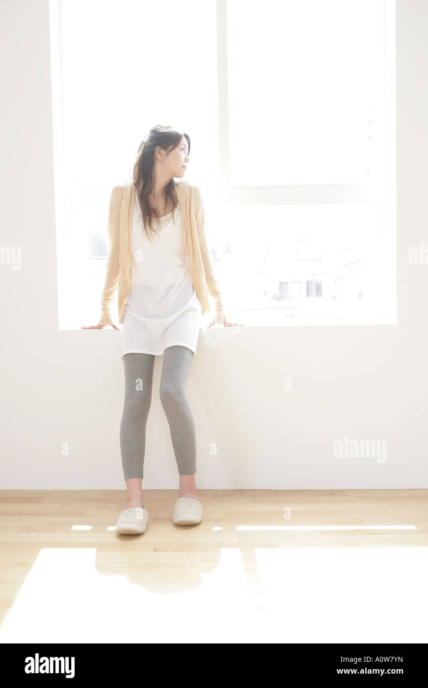 Young woman leaning against a window and thinking Stock Photo - Alamy