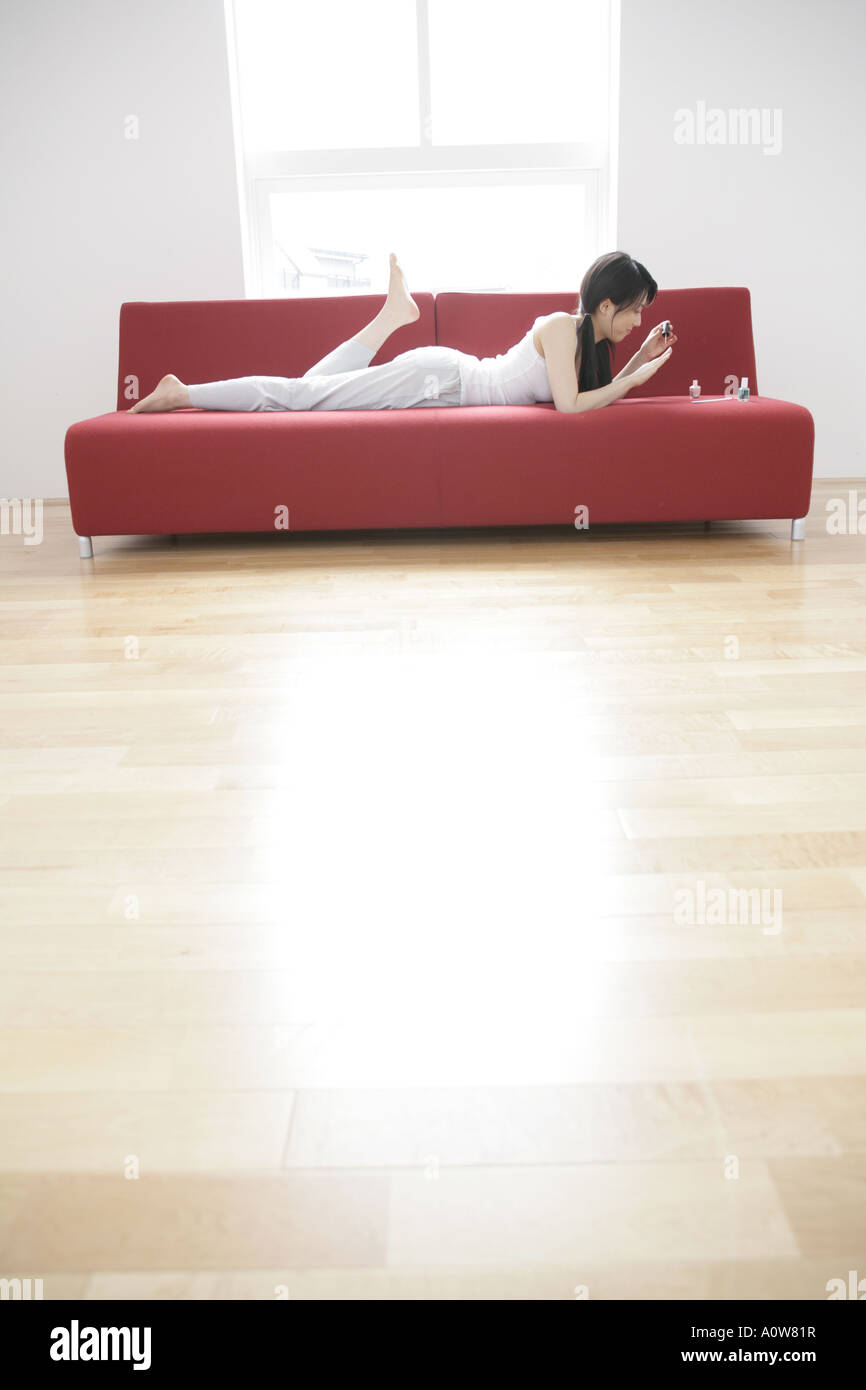 Side profile of a young woman lying on a couch and applying nail polish ...