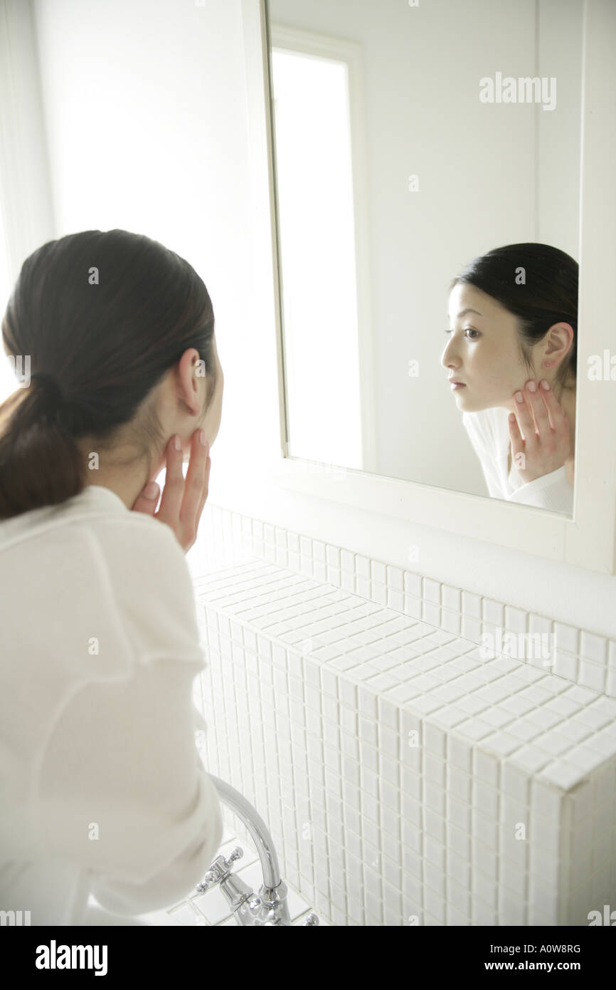 Side profile of a young woman looking into a mirror and touching her ...