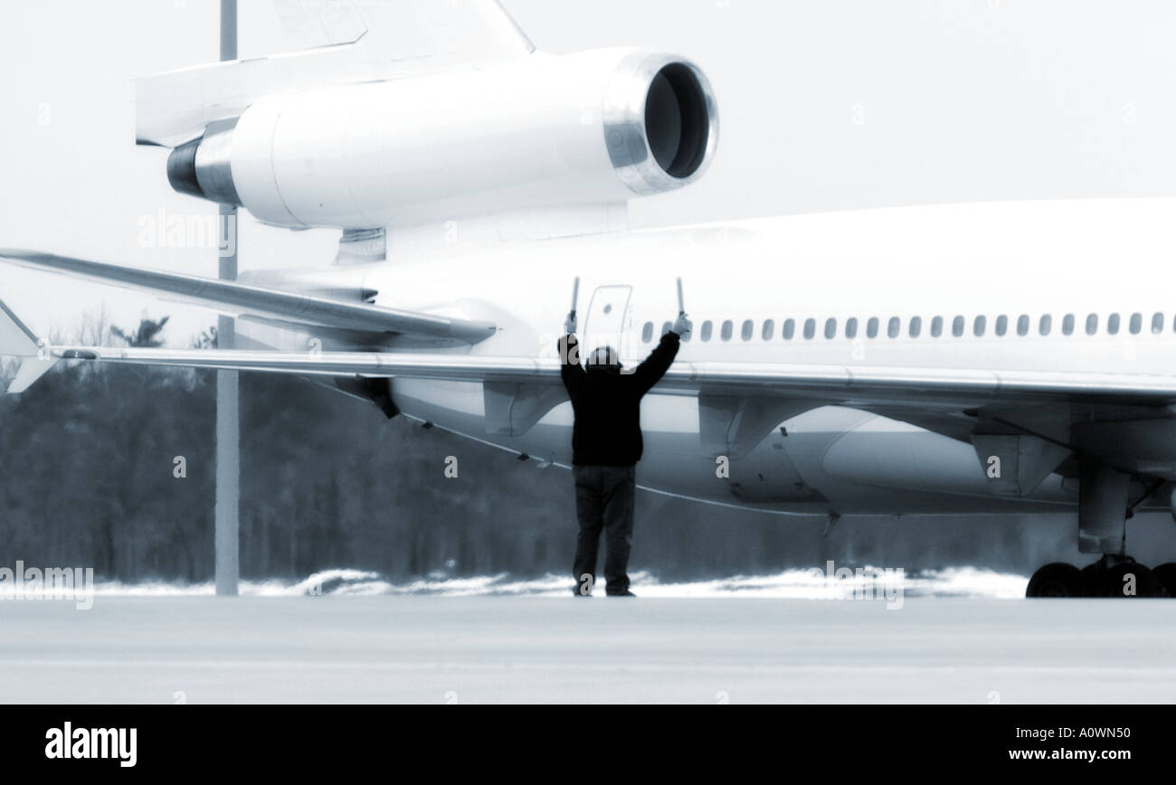 An Airline worker guides a plane on a runway tarmac Stock Photo - Alamy