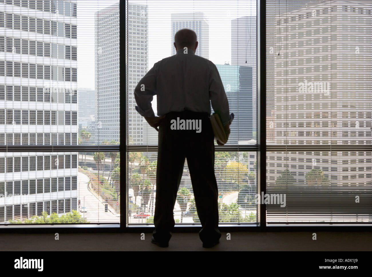 Office worker executive peers out office window looking at downtown Los ...