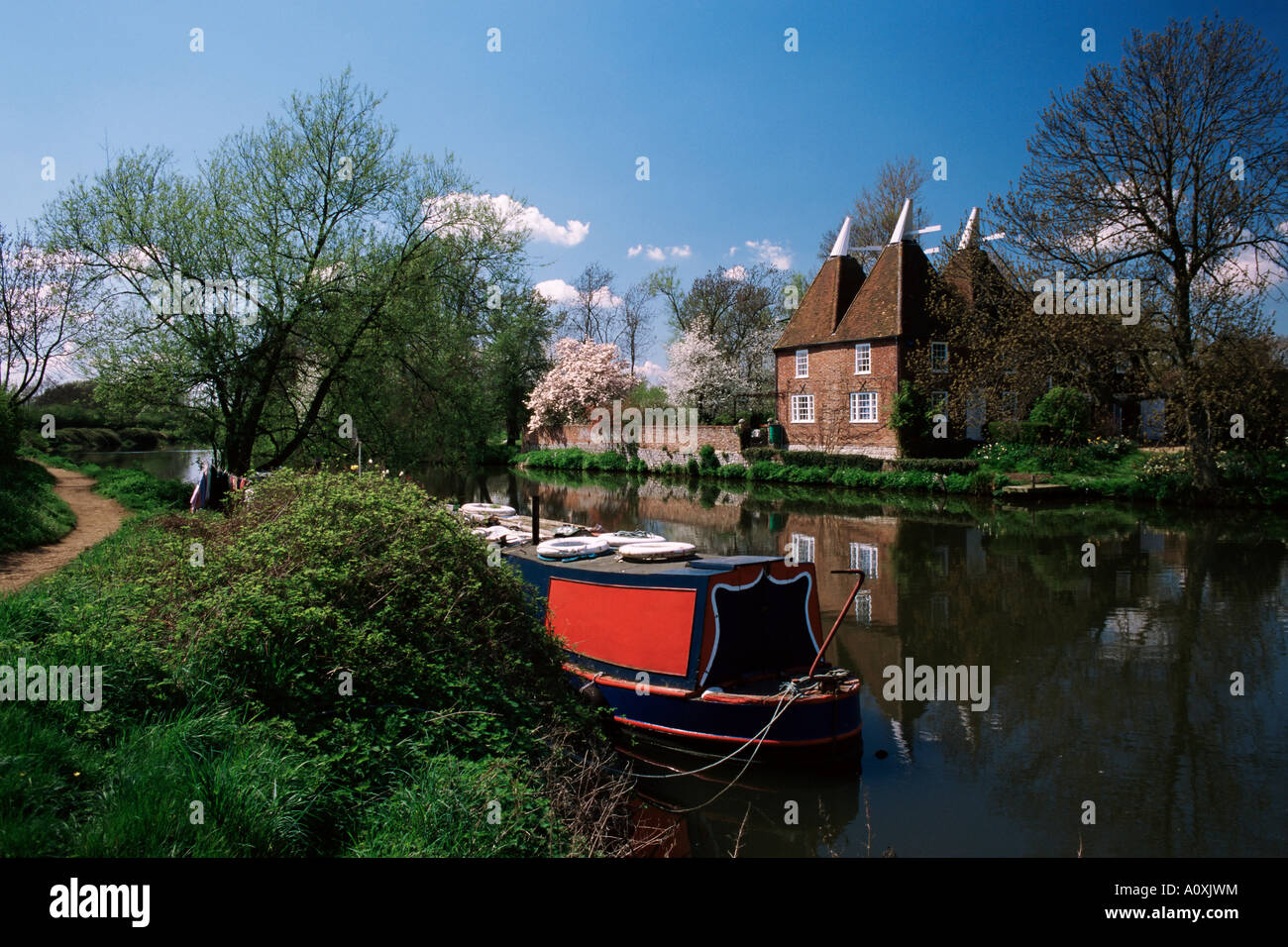 Brightly painted barge and oast houses on the River Medway Yalding near ...
