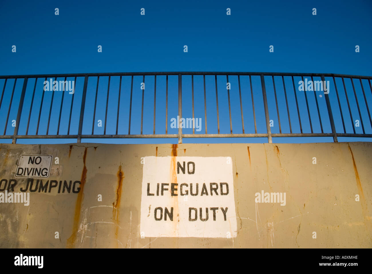 no lifeguard on duty sign on rusty cement wall with handrail against ...