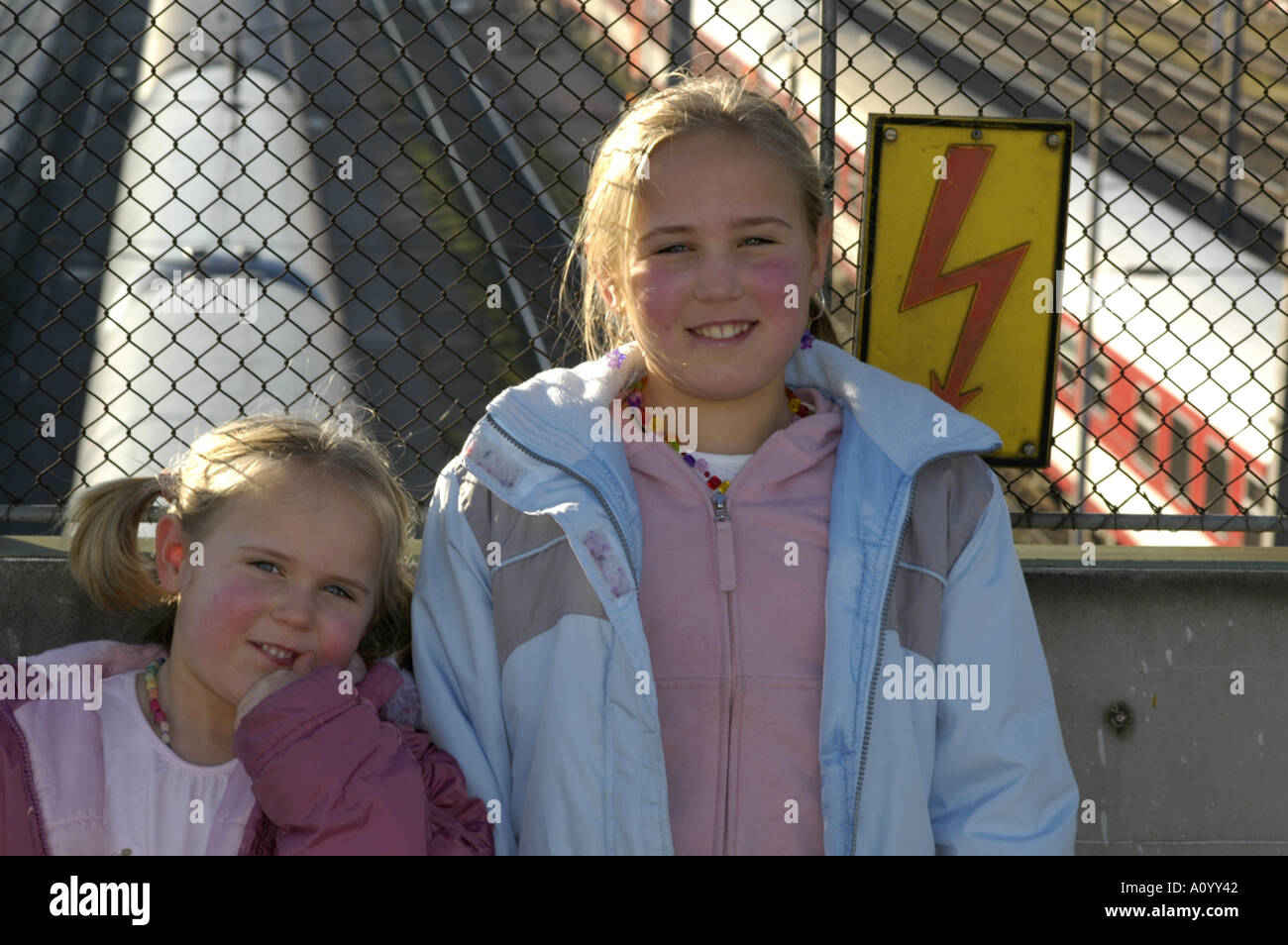 two blond girls in front of a chain-link fence, danger notice Stock ...