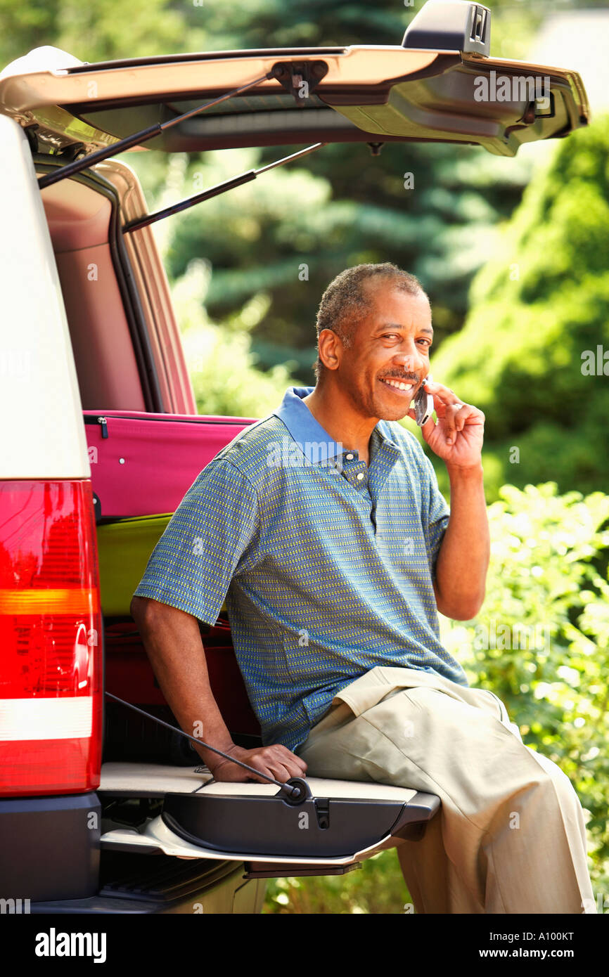 Middle-aged African man talking on his cell phone in trunk of his SUV ...