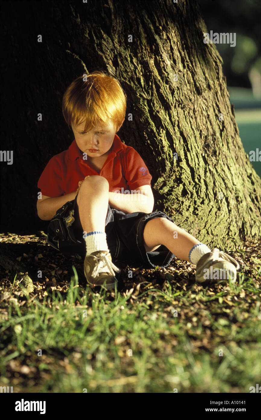 sad red haired little boy sitting in front of a tree Stock Photo - Alamy