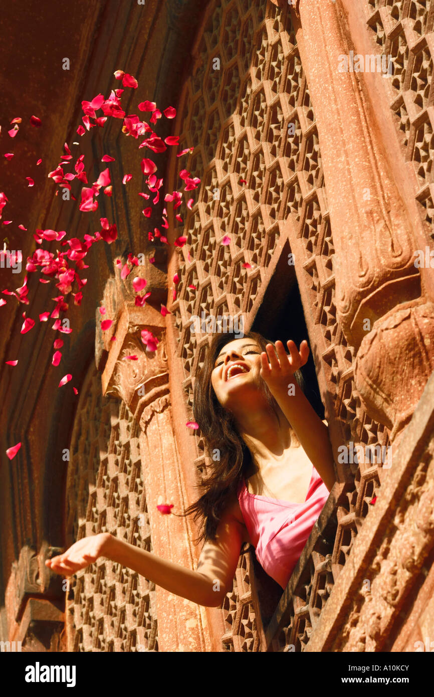 Low angle view of a young woman throwing rose petal from a window, Agra ...