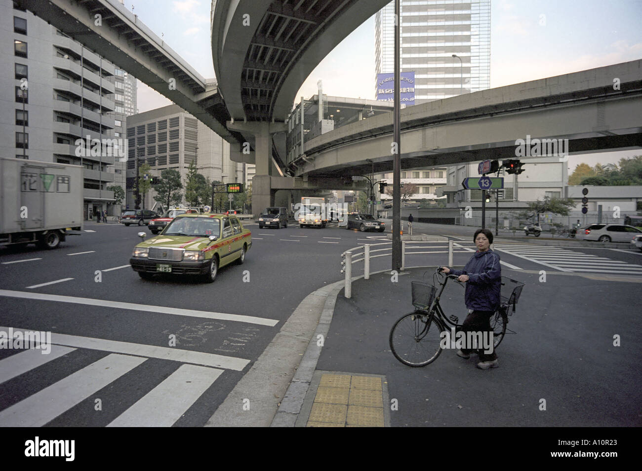 A woman bicyclist wait for a green light to cross a busy Tokyo street ...