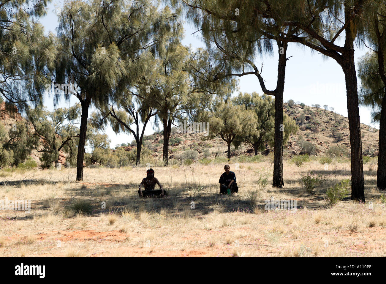Two aboriginal people sit in the shade of a tree near Uluru Ayers Rock ...